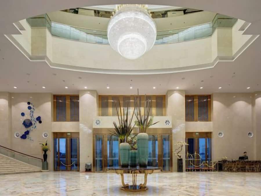 Um hall amplo com um lustre imponente, uma fonte central e uma escadaria que leva aos andares superiores.