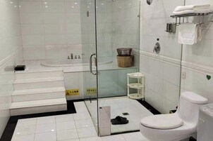 Uma casa de banho com chuveiro em cabine de vidro, banheira branca, sanita e uma pequena prateleira com toalhas.