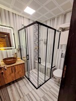 Casa de banho moderna com chuveiro em cabine de vidro, toucador de madeira e chão em mármore.