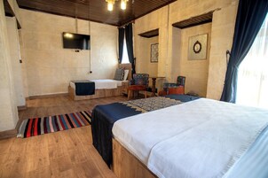 Quarto com cama, escrivaninha, cadeira, televisão e janela com cortinas.