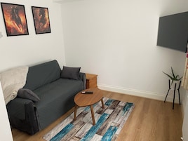 Uma sala de estar moderna com um sofá cinza, uma pequena mesa de apoio de madeira, um tapete azul e branco estampado e duas imagens emolduradas na parede.