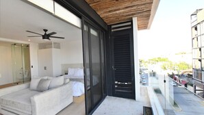 Quarto moderno com sofá-cama, ventilador de teto e porta de vidro deslizante que dá para uma varanda com vista para a rua.