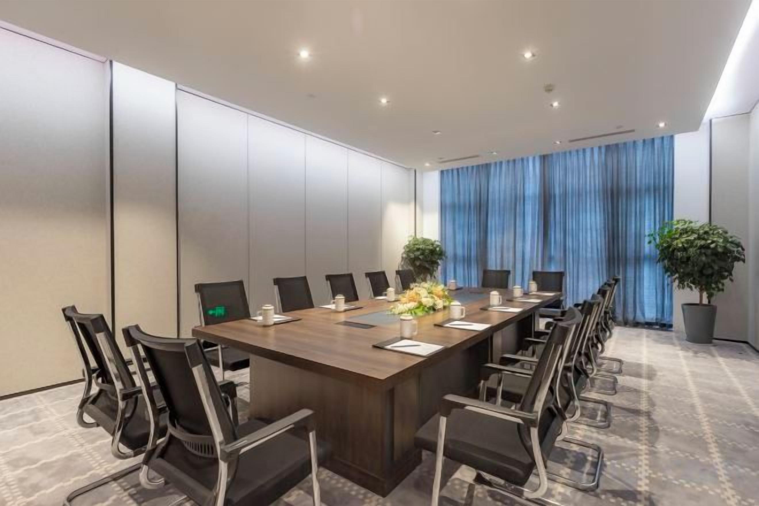Sala de conferência com uma mesa comprida, cadeiras e um vaso de planta.