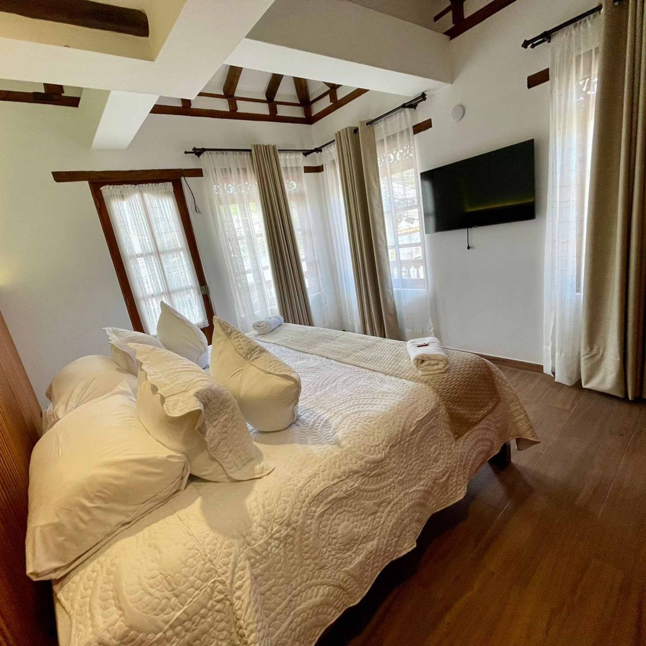 Quarto com cama, cortinas, televisão e vigas de madeira no teto.