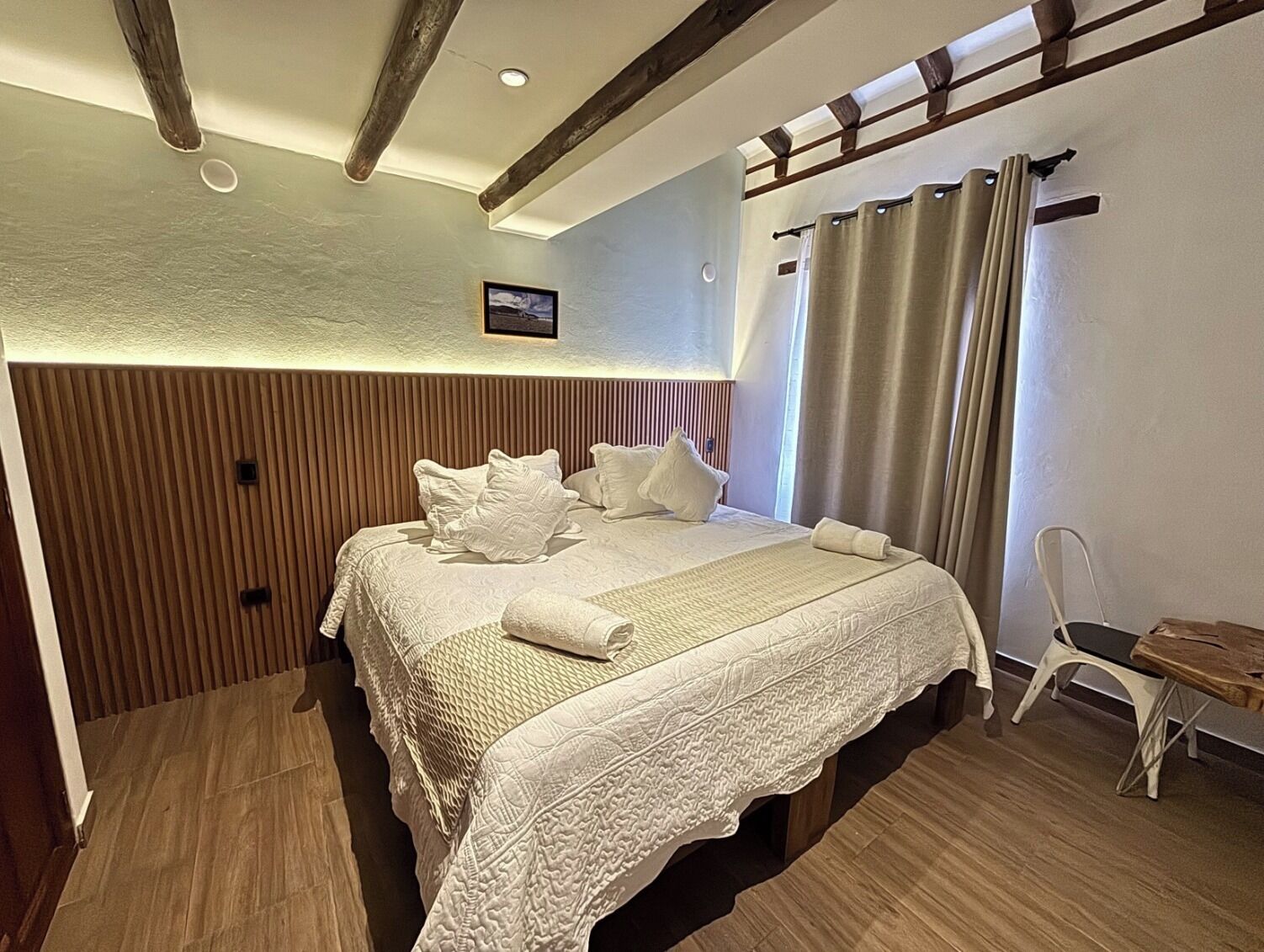 Quarto de hotel com cama, painéis de madeira, uma mesinha e uma cadeira.