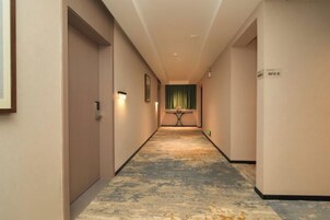 Um corredor de hotel com piso coberto por carpete, portas em ambos os lados e uma mesa com toalha verde ao longe.