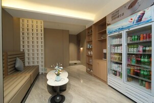 Um saguão de hotel com área de estar, geladeira com bebidas e um vaso decorativo em uma mesa.