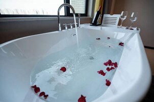 Uma banheira cheia de água e pétalas de rosa, com uma torneira e um porta-objetos com copos e uma garrafa.
