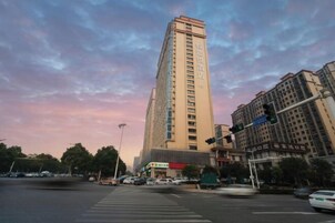 Um edifício alto de hotel com uma placa de destaque, situado num cruzamento movimentado com carros e semáforos.