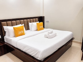 Cama bem arrumada com lençóis brancos, duas almofadas com a marca 'Limetree' e toalhas enroladas.