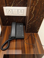 Telefone preto com fio, apoiado em uma escrivaninha de madeira em frente a uma parede com painéis verticais.