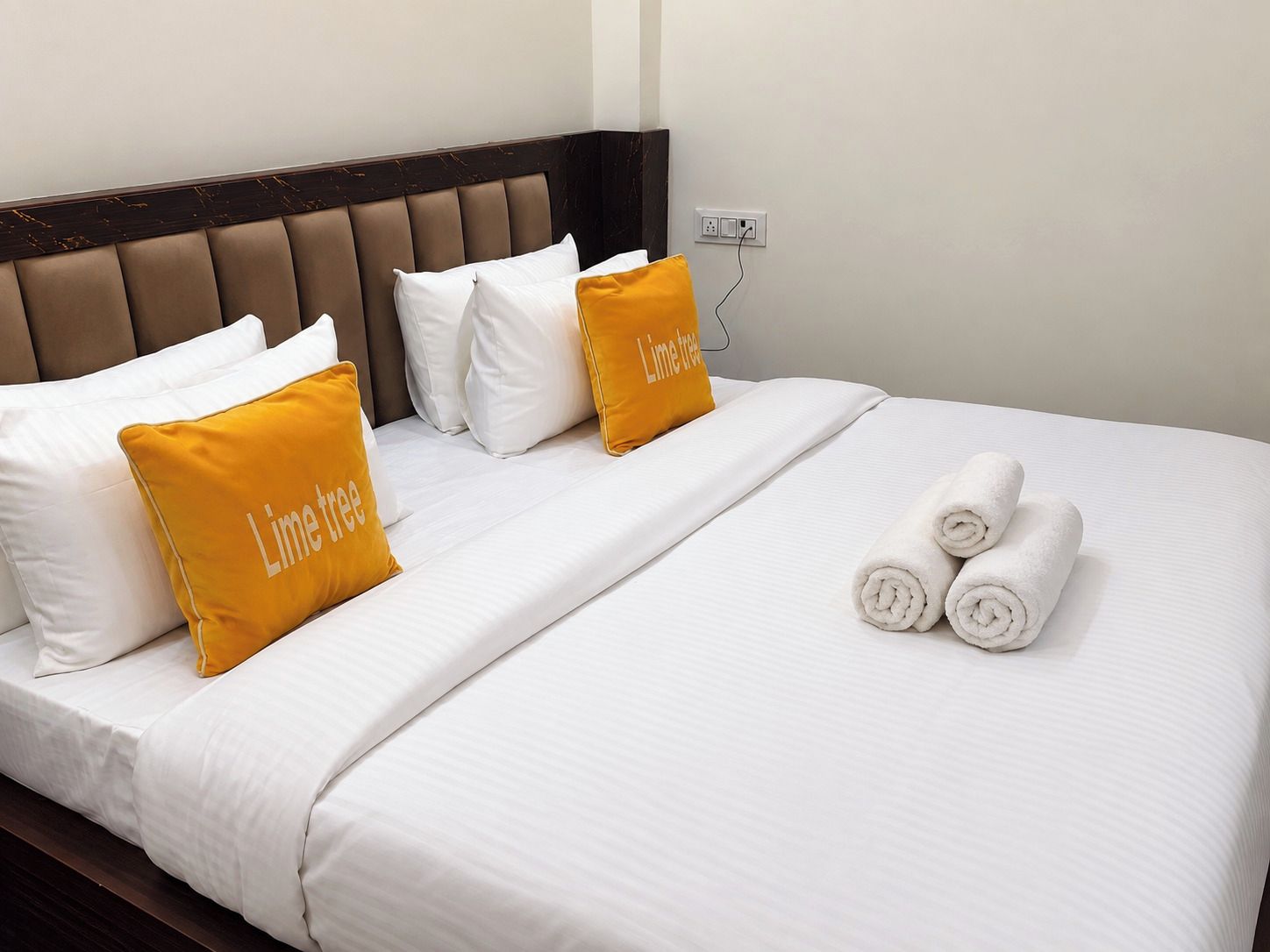 Cama bem arrumada com roupa de cama branca e duas almofadas, uma delas com etiqueta de texto.