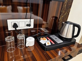 Máquina de café com chaleira, tomada e dois copos sobre uma superfície de madeira.