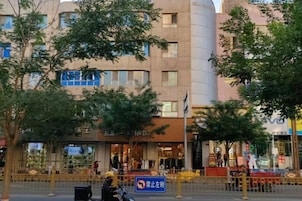 Um edifício de vários andares com fachada moderna, área pedonal com árvores e placa indicando zona proibido estacionar.