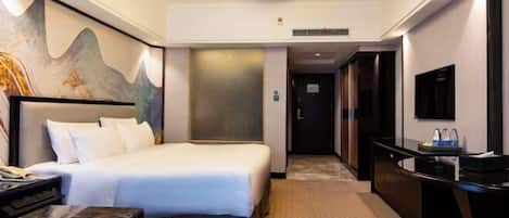 Quarto de hotel com cama, escrivaninha, cadeira, televisão e um quadro na parede.