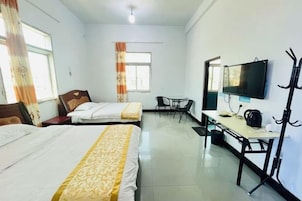 Quarto de hotel com duas camas, uma escrivaninha, uma cadeira, uma televisão e um cabideiro.