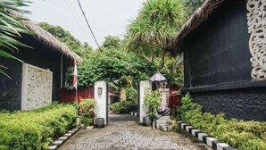 Um caminho estreito e pavimentado, ladeado por vegetação exuberante e edifícios tradicionais com telhados de palha.