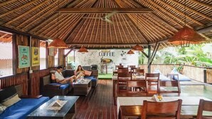 Um café ao ar livre com móveis de madeira e um telhado de palha.