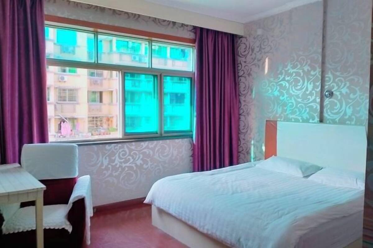 Quarto de hotel com cama, cadeira, mesa e janela com cortinas.
