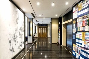 Um corredor com parede de mármore, uma porta e uma parede repleta de livros.