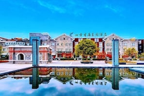 Um edifício refletido em um espelho d'água, rodeado por árvores e outros edifícios.