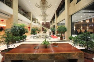 Um hall amplo com uma mesa de madeira central, plantas em vasos e um lustre.