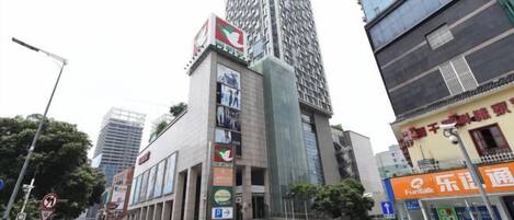 Edifício de vários andares com uma placa grande no topo, cercado por outros edifícios e uma faixa de pedestres.