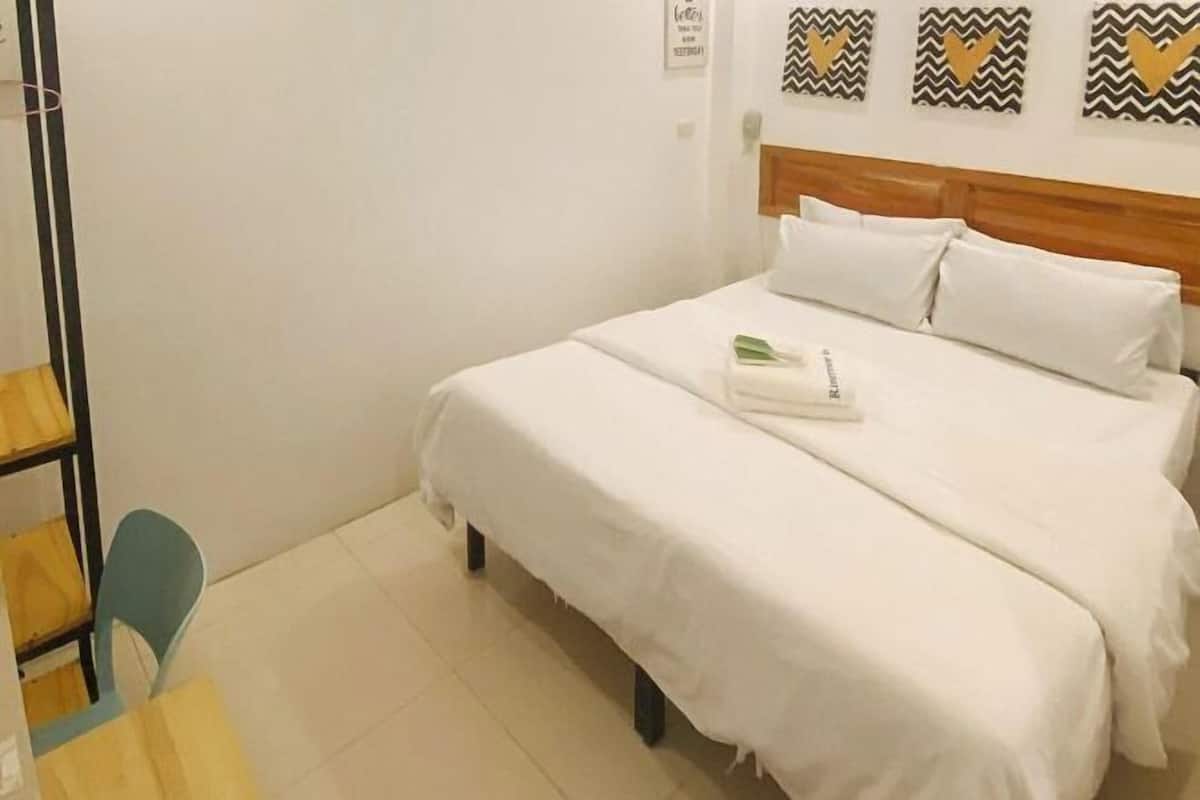Uma cama de solteiro com roupa de cama branca, cabeceira de madeira e uma pequena mesa de cabeceira com abajur.