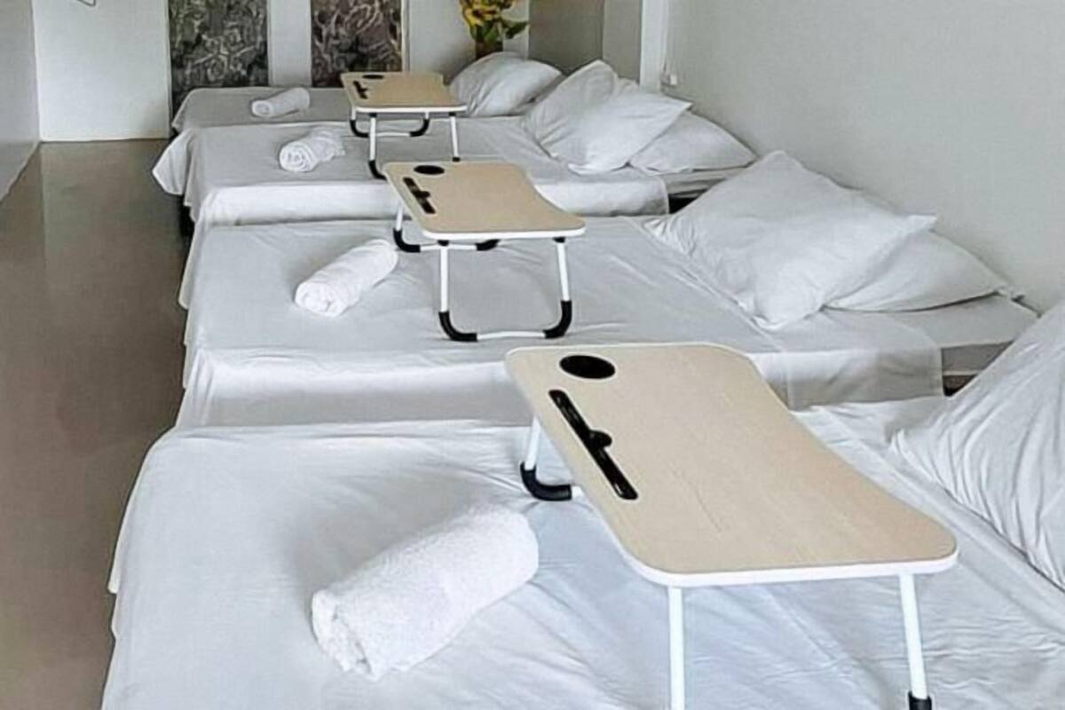 Quarto de hotel com três camas, cada uma com mesa de cabeceira de madeira e roupa de cama branca.