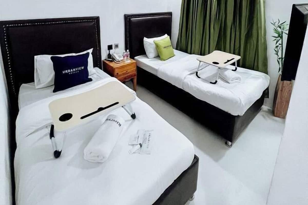 Quarto de hotel com duas camas, cada uma com cabeceira, mesa de cabeceiro e travesseiro com o nome do hotel.