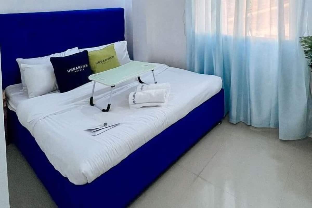 Cama com roupa de cama branca, cabeceira azul e mesa de cabeceira com bandeja.