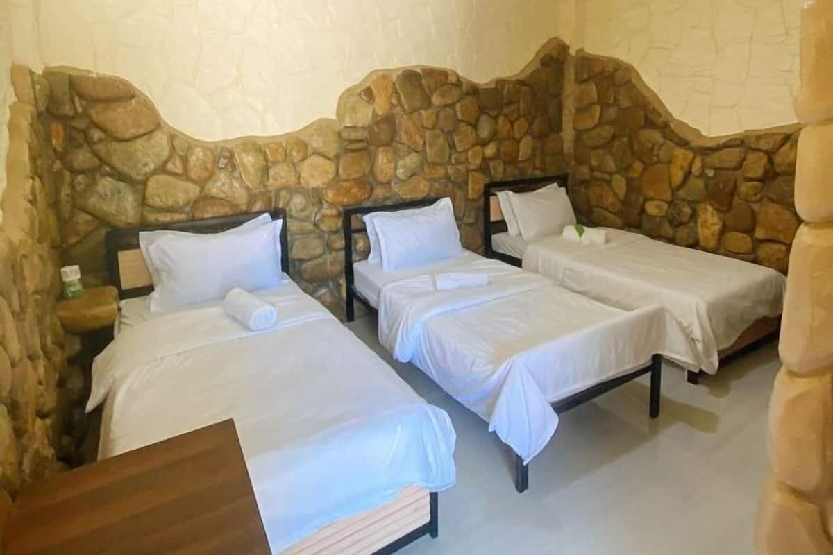Quarto com três camas de solteiro encostadas a uma parede de pedra, cada uma com roupa de cama e almofadas brancas.