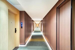 Corredor longo e estreito de hotel com paredes de madeira e piso coberto de carpete.