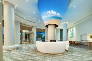 Um saguão de hotel com uma recepção central, teto curvo e entrada de vidro.