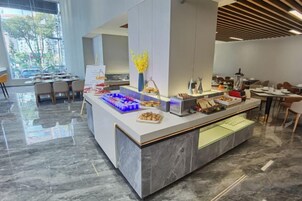 Espaço de refeições moderno com piso de mármore, balcão de buffet com diversos alimentos e vista para o exterior.
