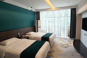 Quarto de hotel com duas camas, uma janela grande com cortinas, uma TV de tela plana e piso coberto de carpete.