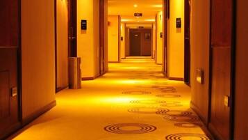 Corredor de hotel com portas em ambos os lados, carpete estampado e iluminação no teto.