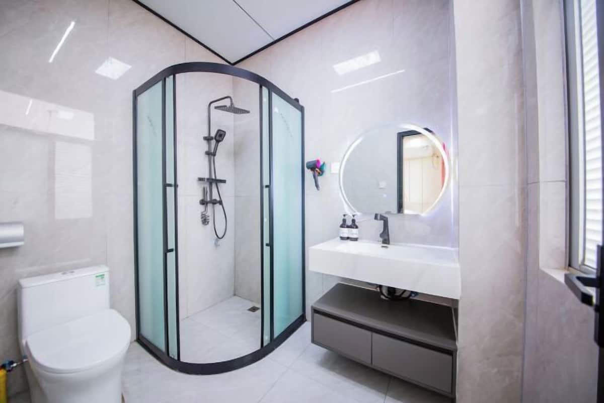 Casa de banho moderna com cabine de duche em vidro, sanita branca e toucador com espelho.