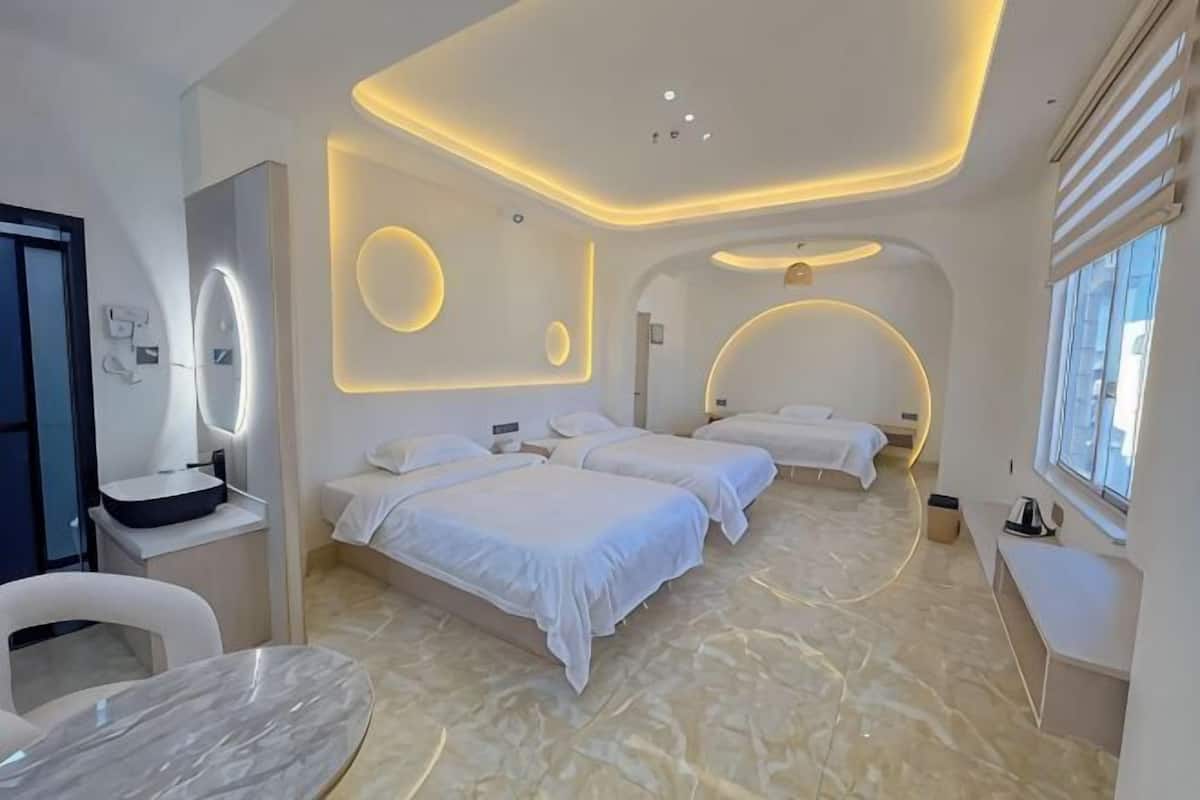 Quarto de hotel moderno com piso de mármore, duas camas, um espelho redondo, uma escrivaninha e uma janela.