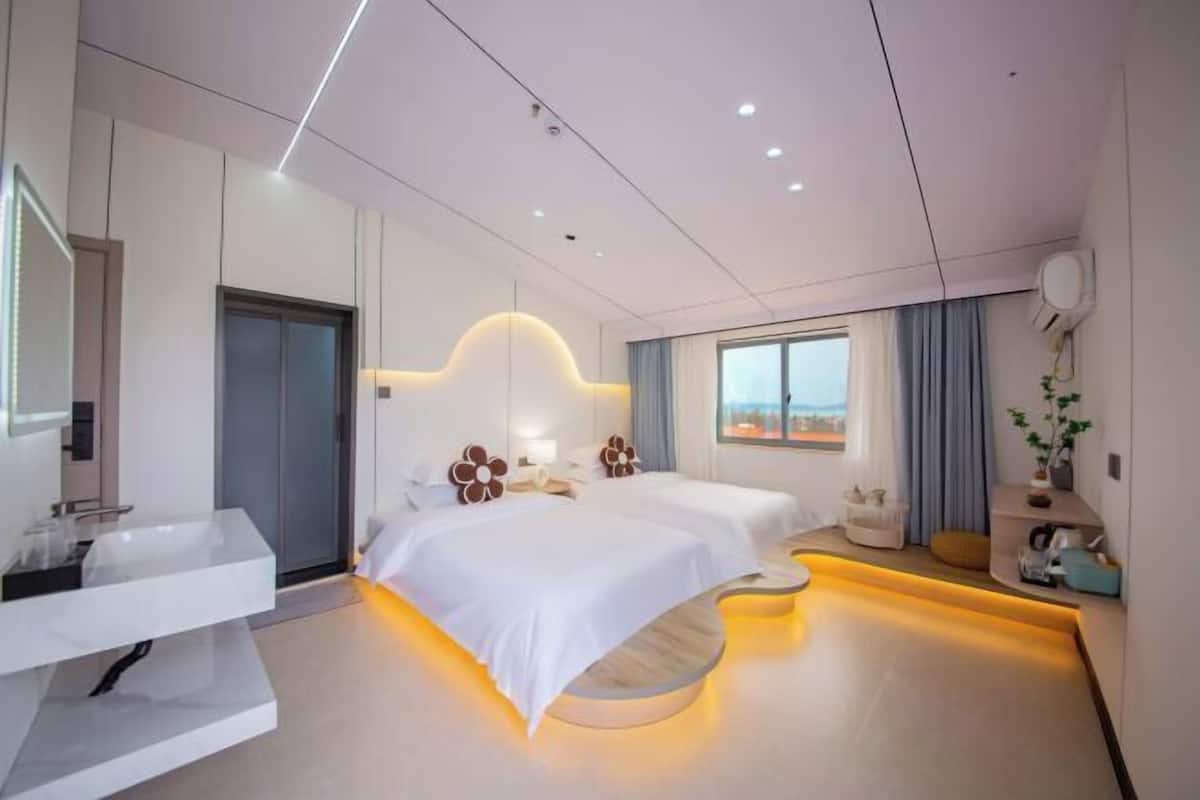 Quarto de hotel moderno com uma cama grande, área de estar separada, banheiro com pia branca e vista para a cidade.
