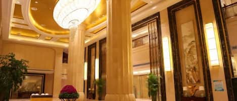 Um saguão com uma luminária circular grande, um balcão de recepção e um pilar imponente.
