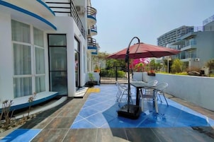 Varanda de hotel com mesa, cadeiras e um guarda-sol vermelho.