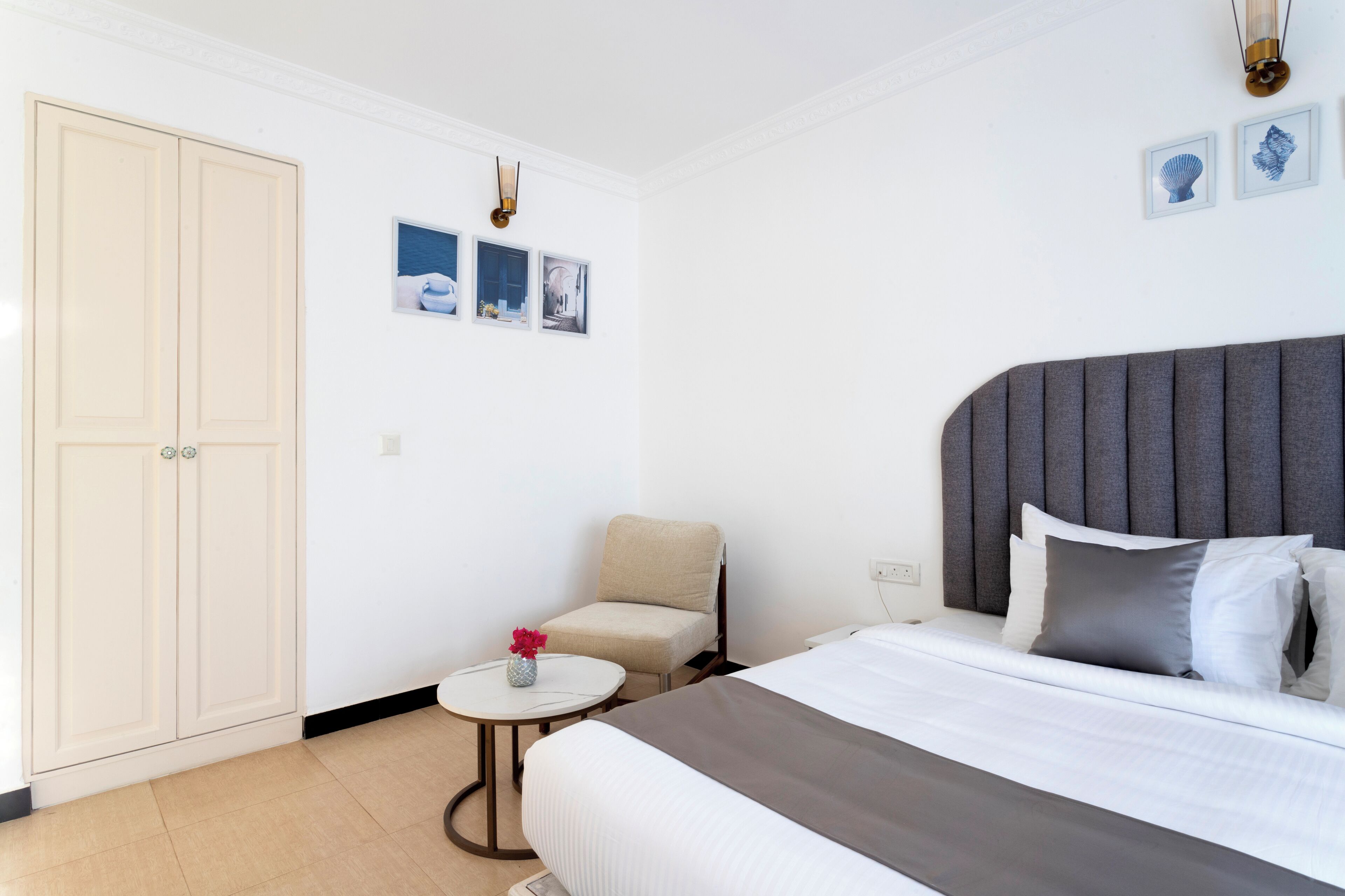 Quarto de hotel com cama, uma cadeira, uma mesinha e um guarda-roupa.