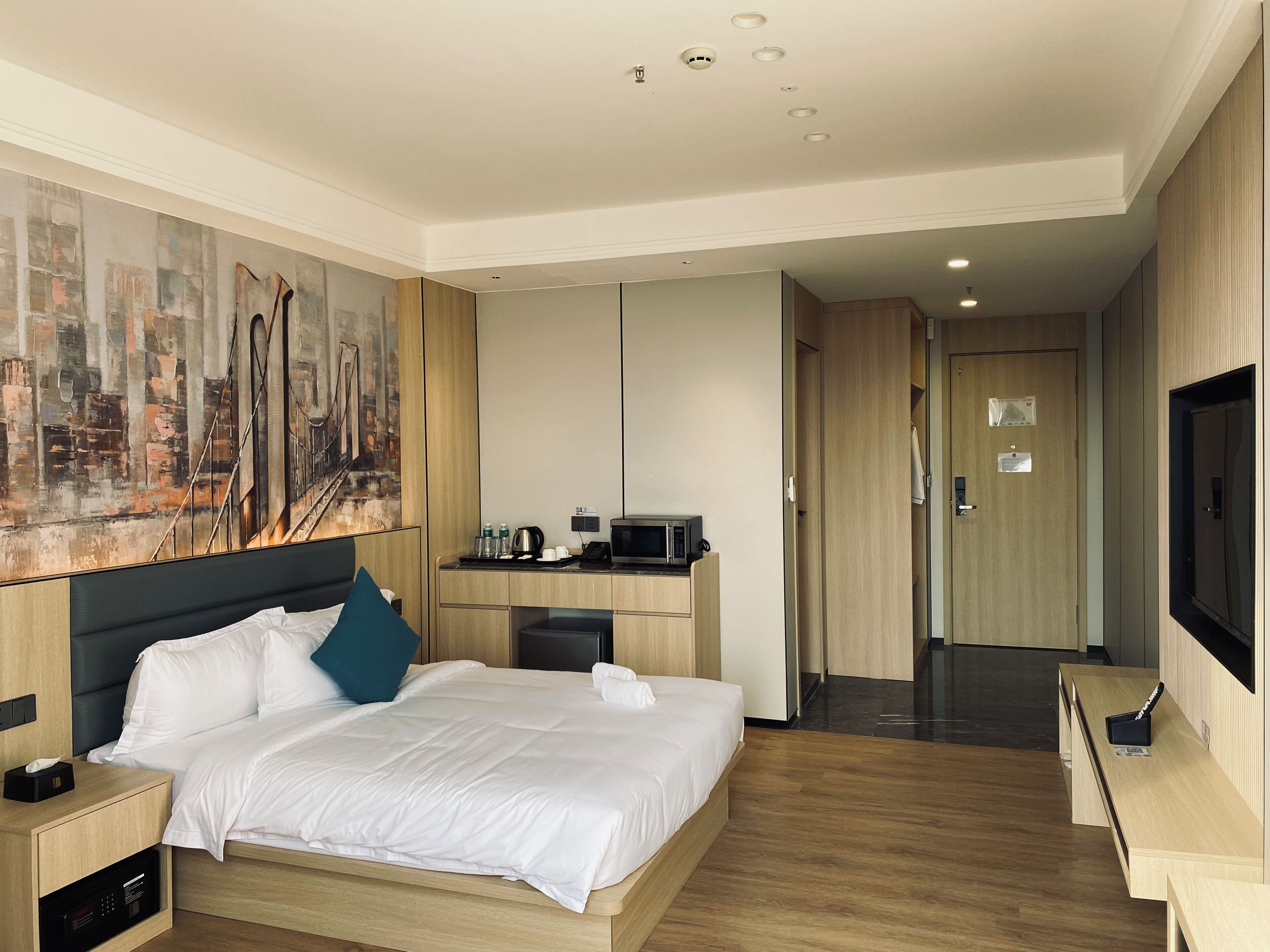 Quarto de hotel com cama, escrivaninha, micro-ondas, pintura e televisão.