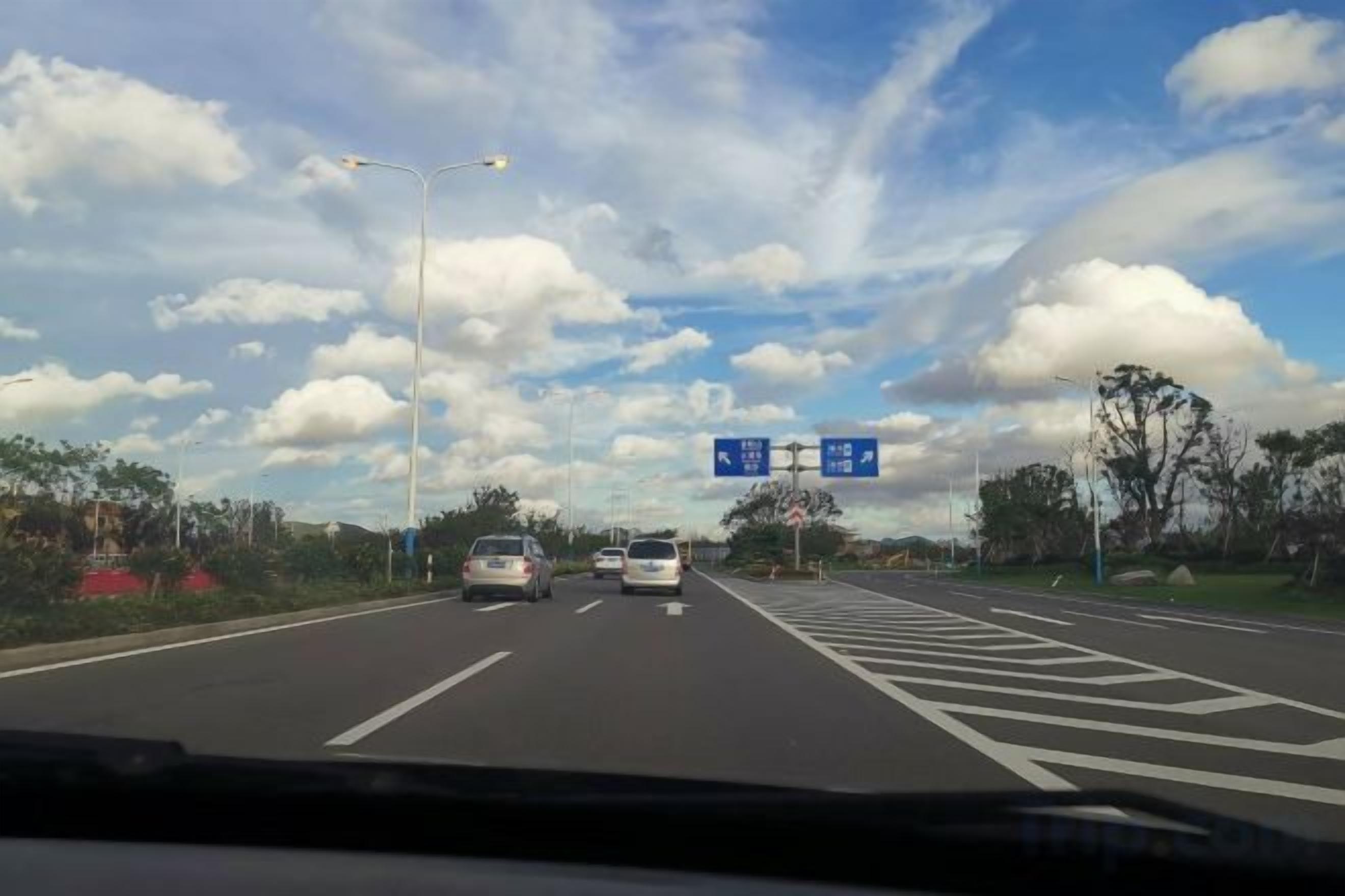 Autoestrada com múltiplas faixas, veículos, placas de sinalização e céu claro.
