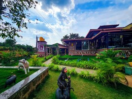 Um edifício tradicional com desenhos elaborados nas paredes, um jardim bem cuidado com diversas plantas e uma estátua de macaco.