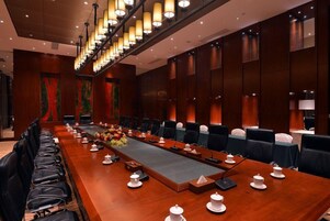Uma sala de conferências com uma mesa comprida, cadeiras e uma fileira de luminárias.