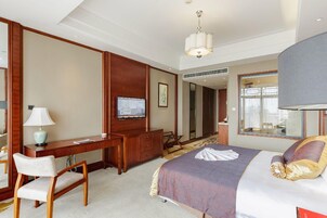 Quarto de hotel com cama, escrivaninha, cadeira, televisão e um espelho grande.