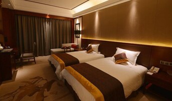 Quarto de hotel com duas camas, uma escrivaninha, uma cadeira e uma janela grande com cortinas.