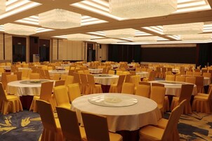 Salão de banquetes com mesas redondas e cadeiras, equipado com lustres e uma tela de projeção.